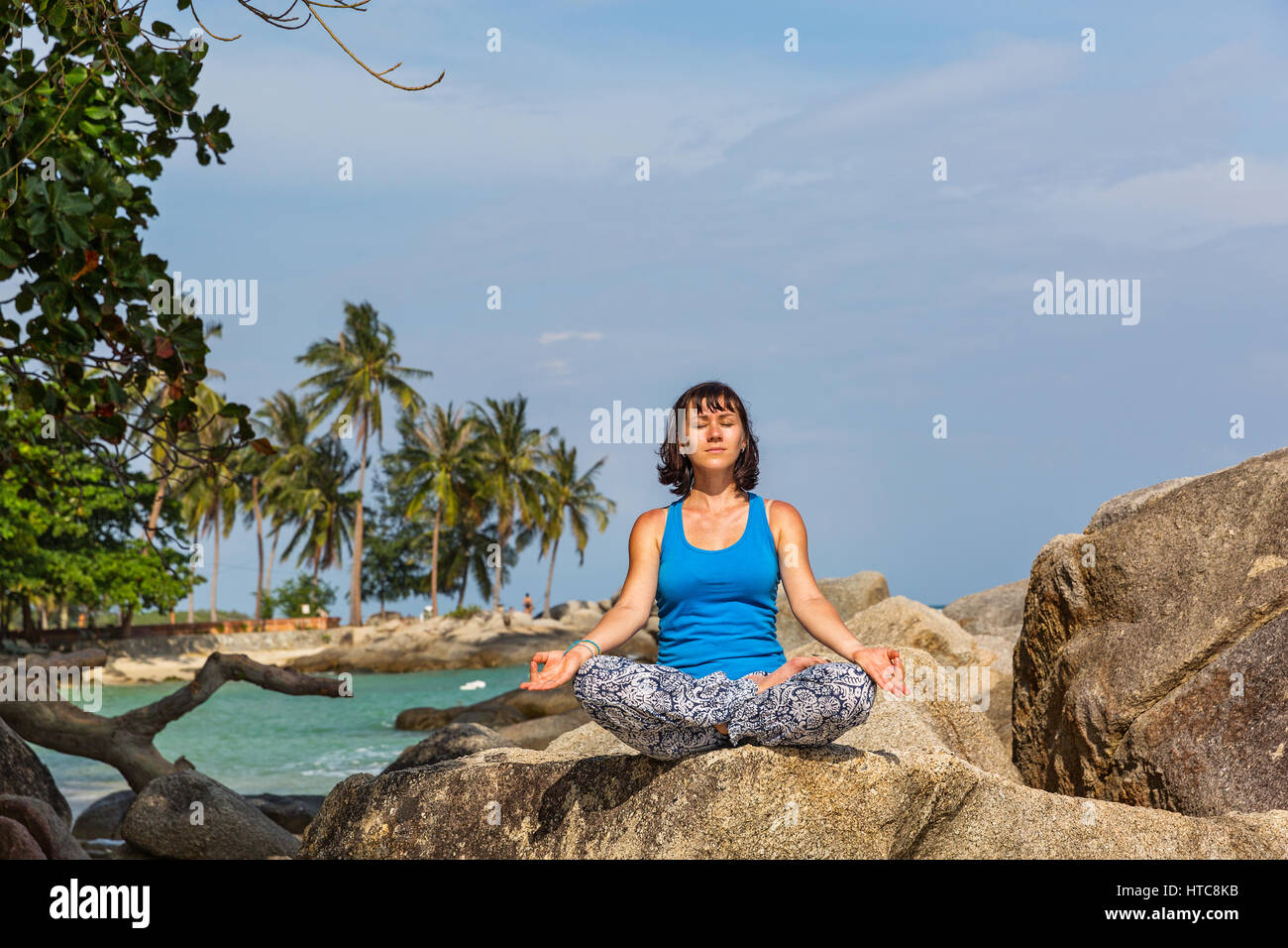 Woman sitting on a rock on the beach in Lotus pose and doing yoga Stock ...