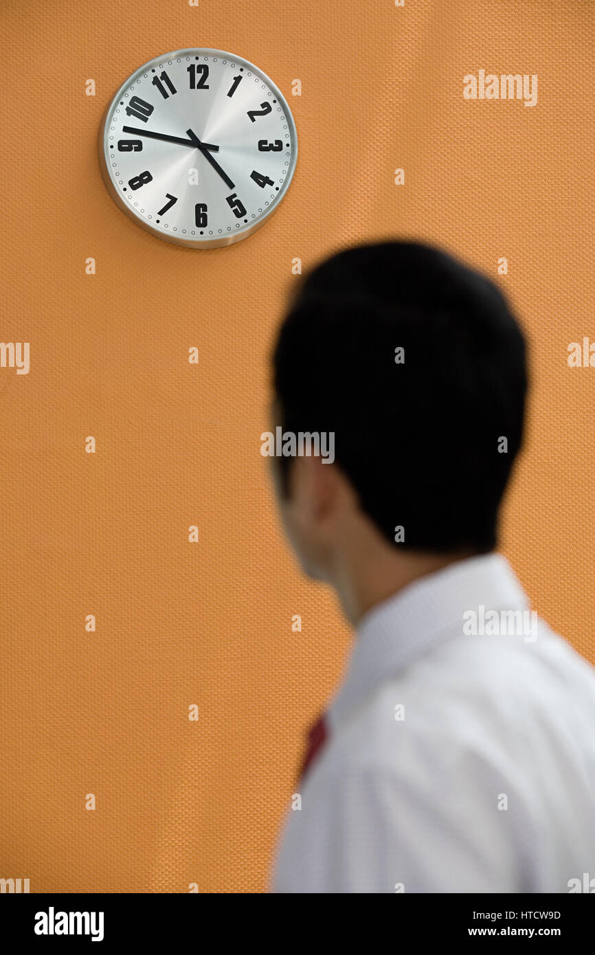 Office worker looking at a wall clock Stock Photo - Alamy