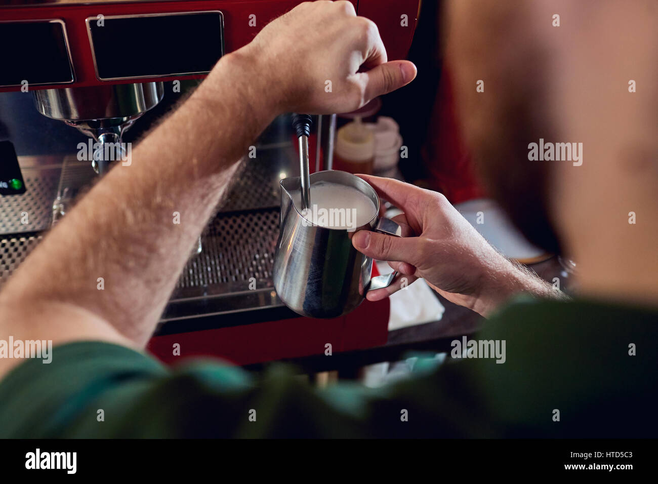 Bartender, barista makes hot milk in a coffee machine behind the bar ...