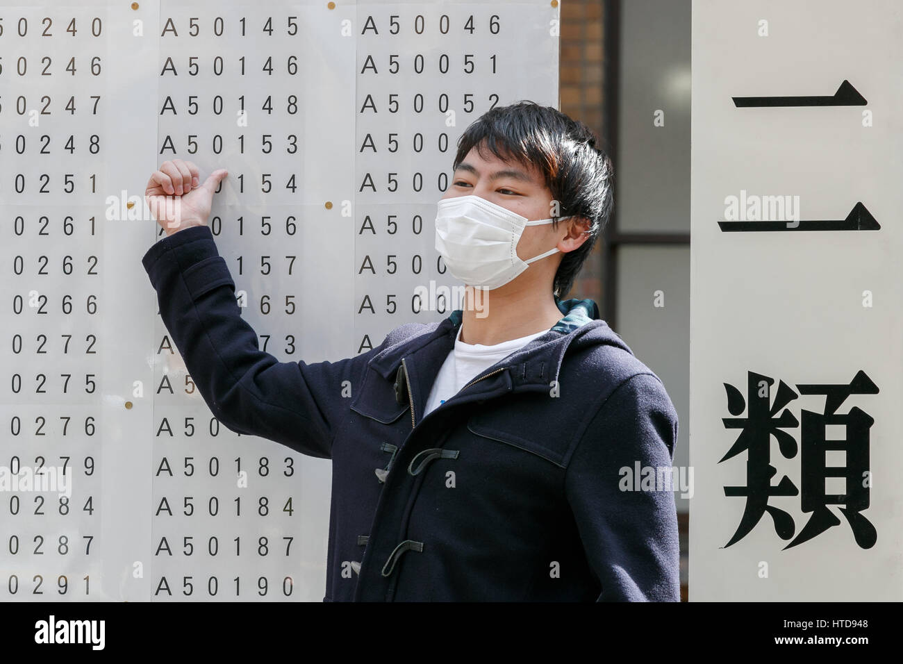 A Japanese student points his exam number on the list at the University ...