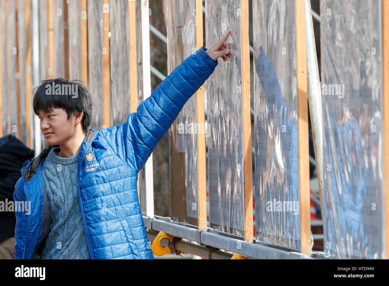 A Japanese student points his exam number on the list at the University ...