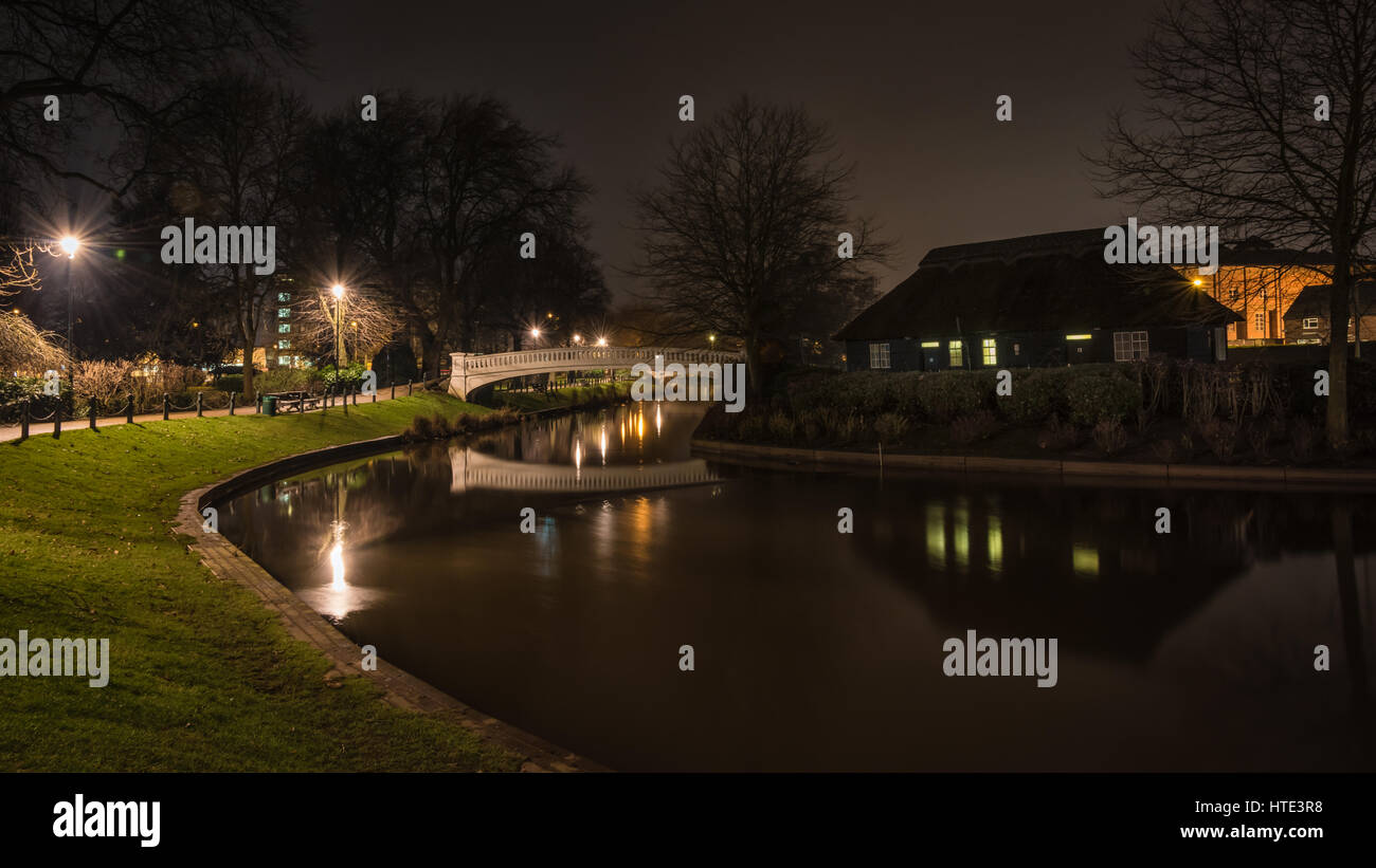A night time photograph of a river running through a town park with a ...