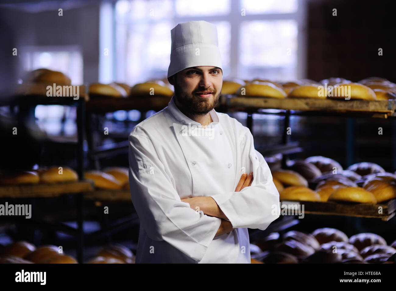 young handsome man baker in white uniform and cap on background bakery ...