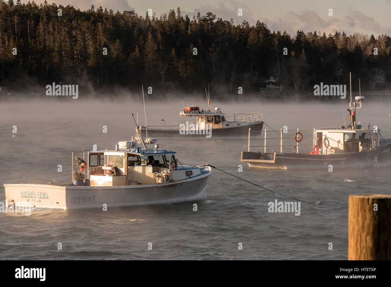 Sea smoke rises from the surface and surrounds lobster boats with ...