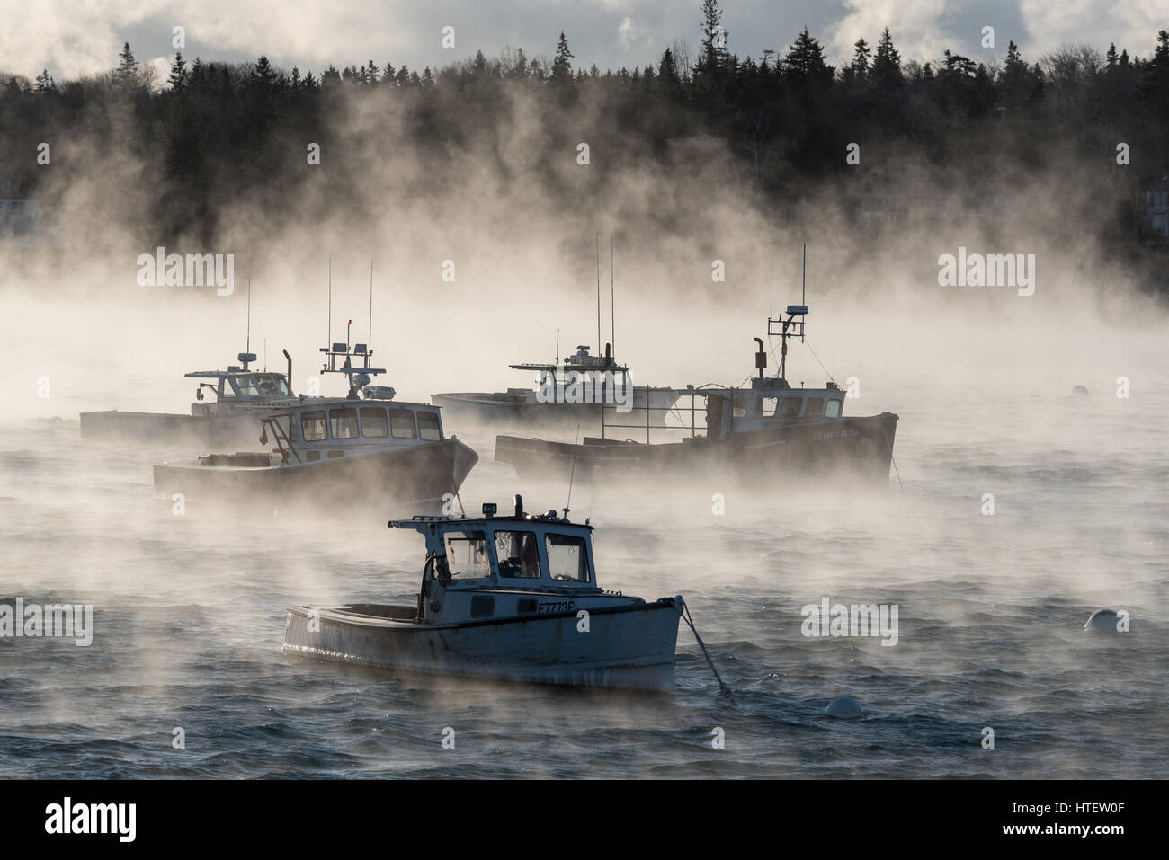 Sea smoke rises from the surface and surrounds lobster boats with ...
