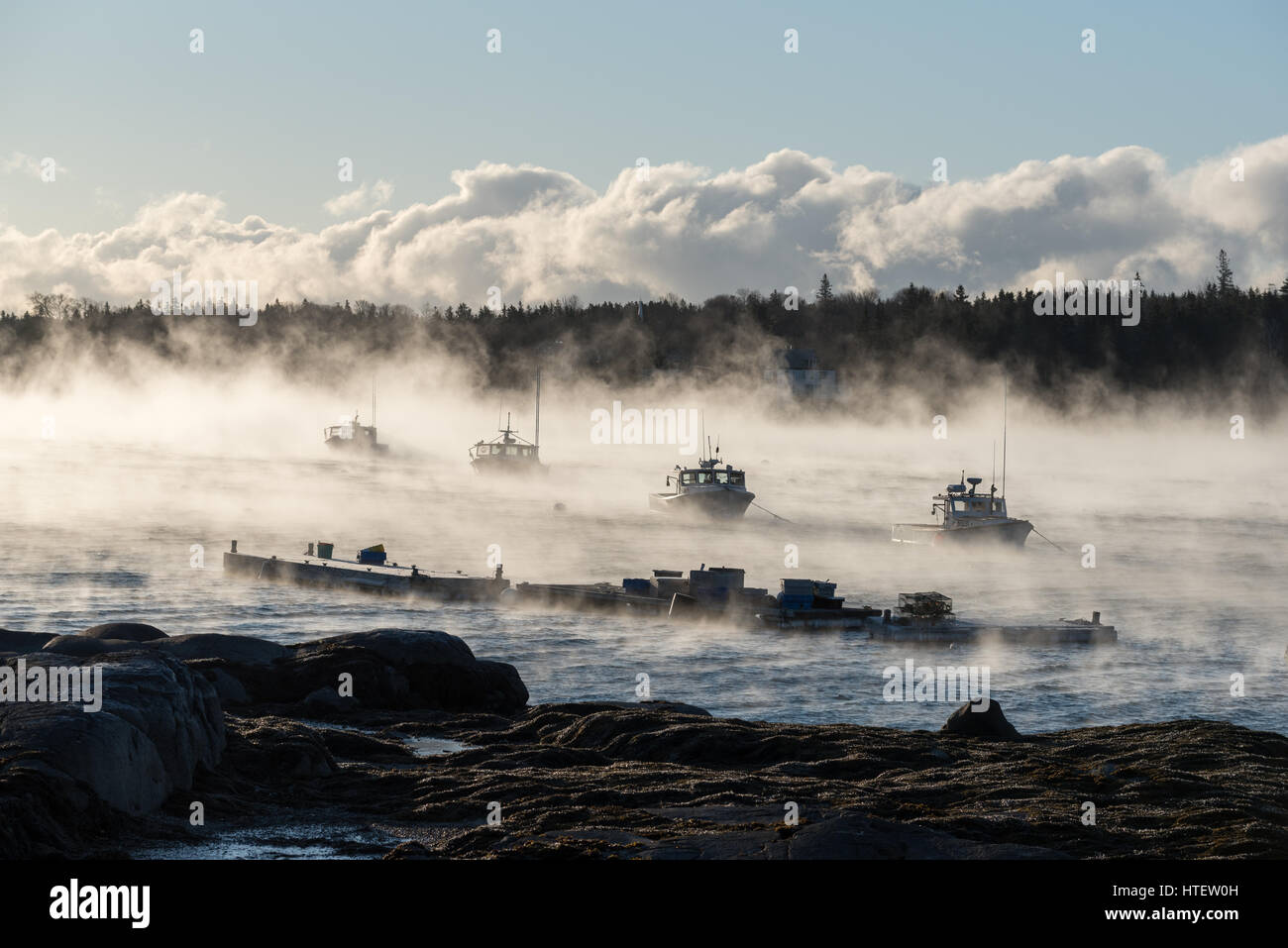 Sea smoke rises from the surface and surrounds lobster boats with ...