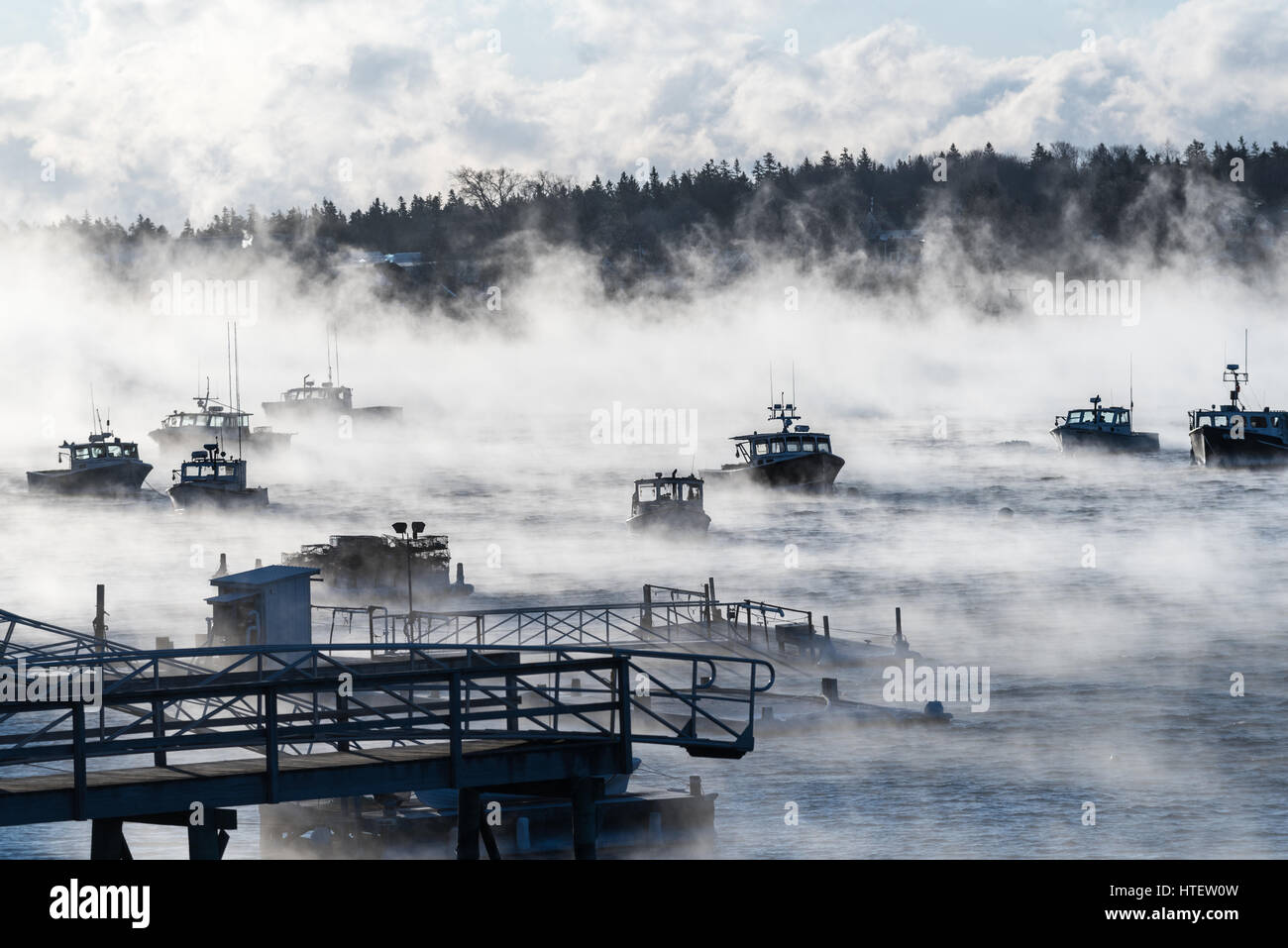 Sea smoke rises from the surface and surrounds lobster boats with ...