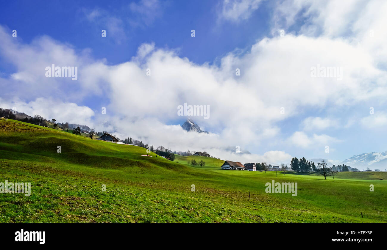 Alpine natural landscape with green fields, high rocks and white clouds ...