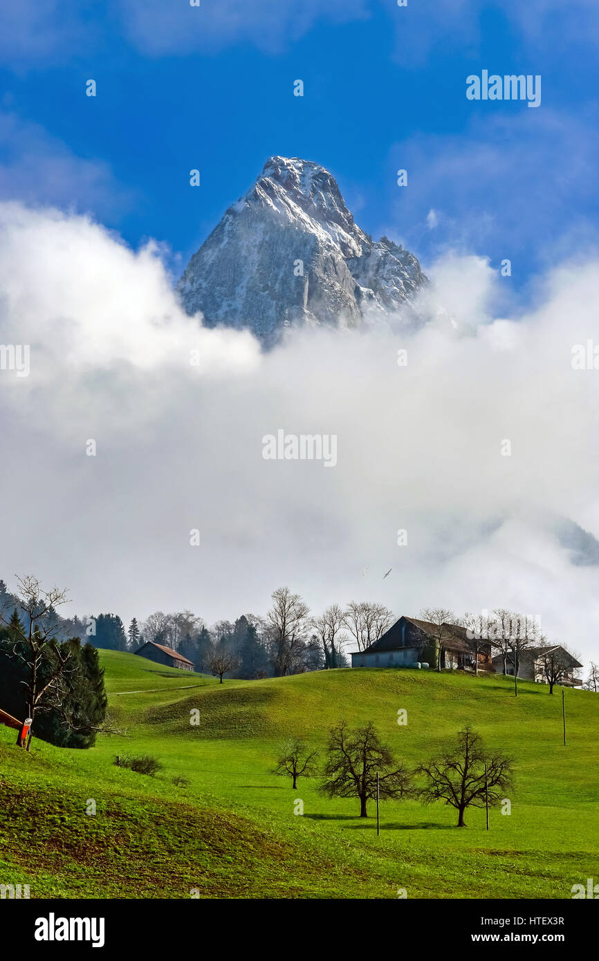Alpine natural landscape with green fields, high rocks and white clouds ...
