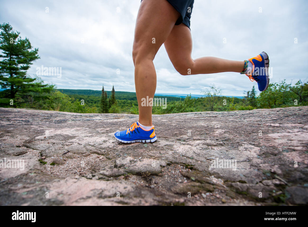 Legs of a young woman wearing fitness clothing running across rocks ...
