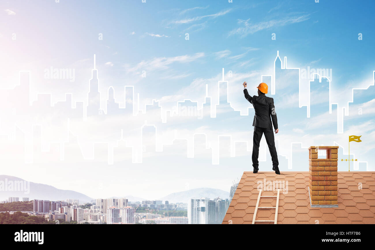 Engineer man standing with back on house roof and drawing city. Mixed ...