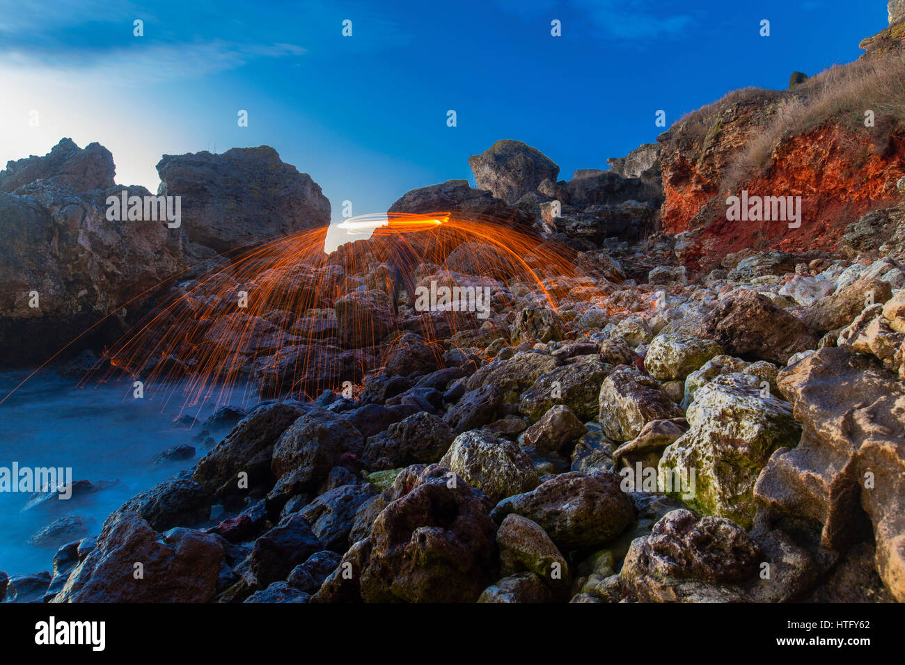 Man rotating fire on rocky shore Stock Photo - Alamy