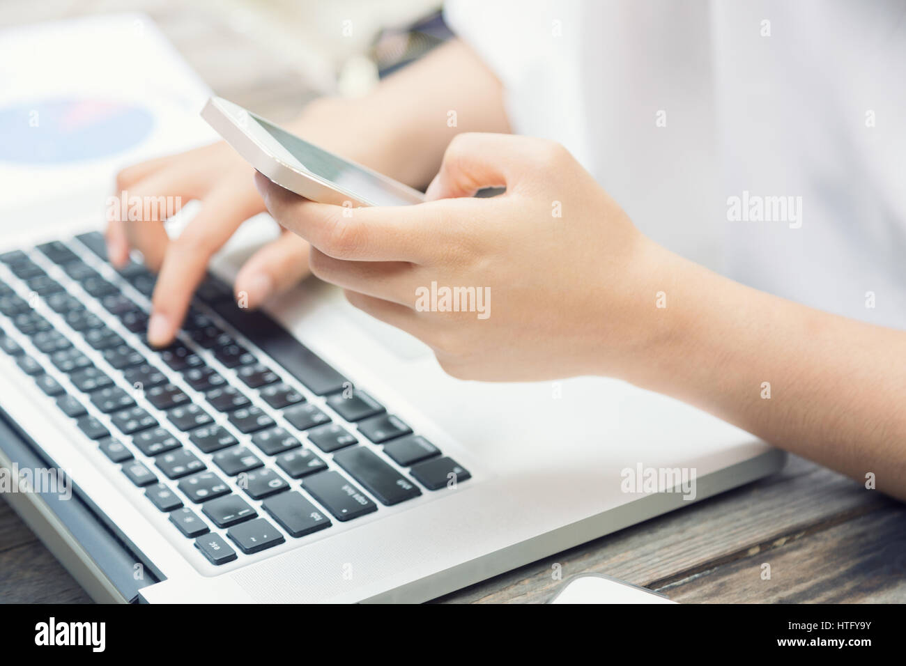 Female hands on laptop keyboard and holding smart phone, selective ...