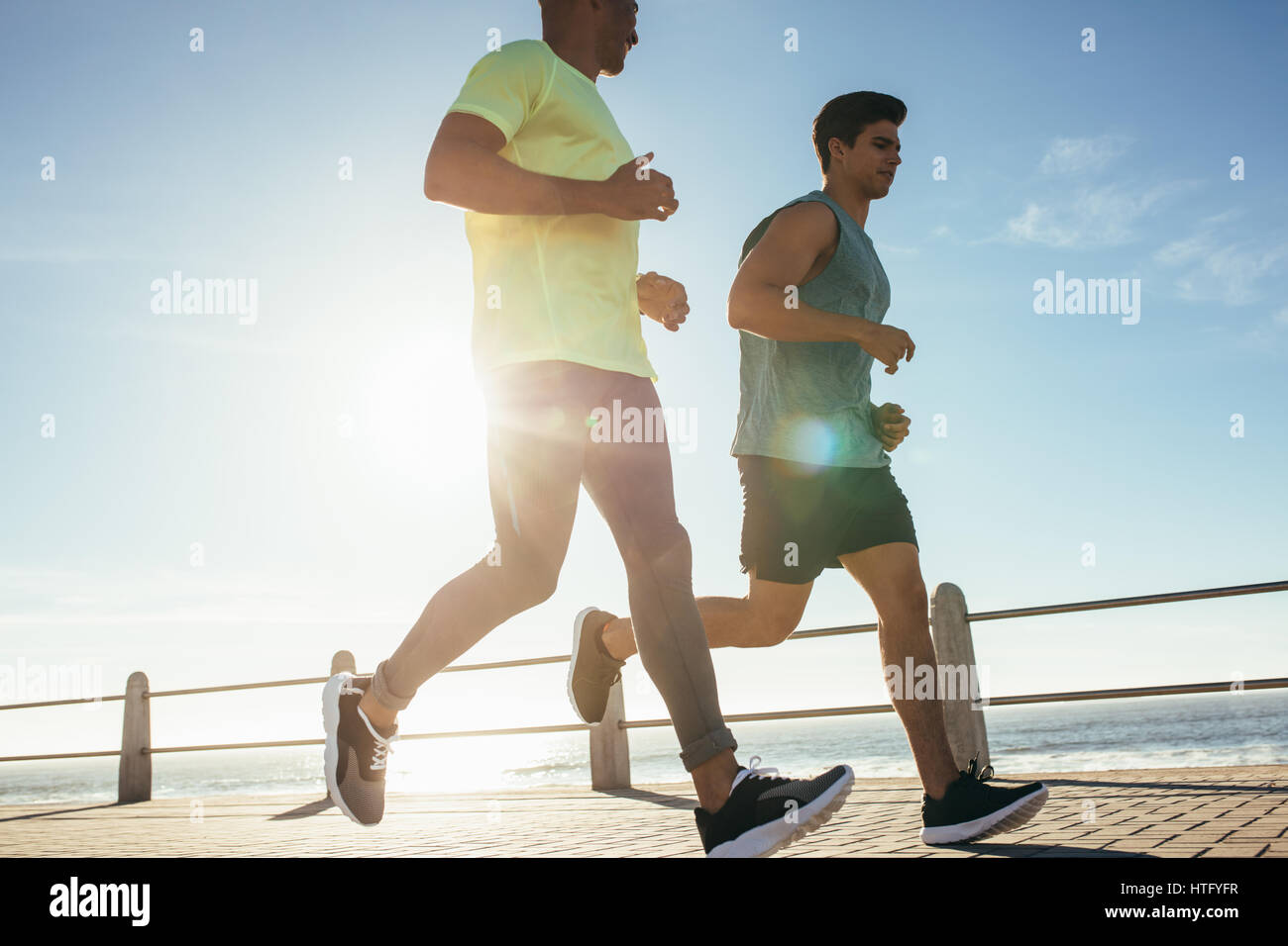 Low angle shot of two young men running on sea front. Fit young runner ...