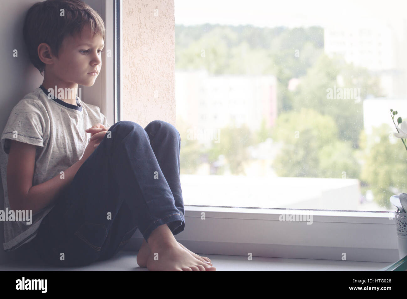 Sad kid sitting on window shield and looking out the window Stock Photo ...