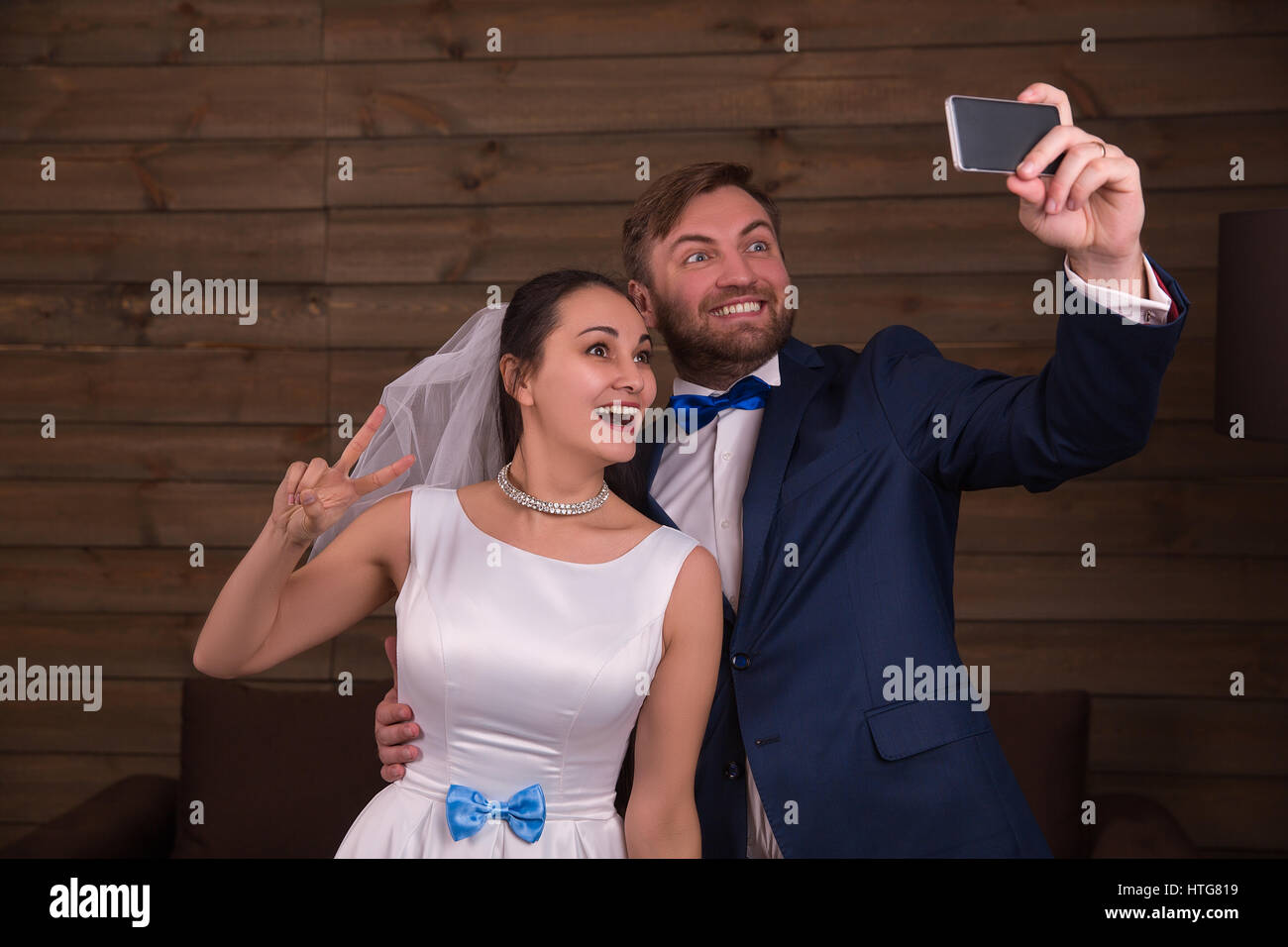 Smiling bride and groom making selfie on mobile phone, wooden ...