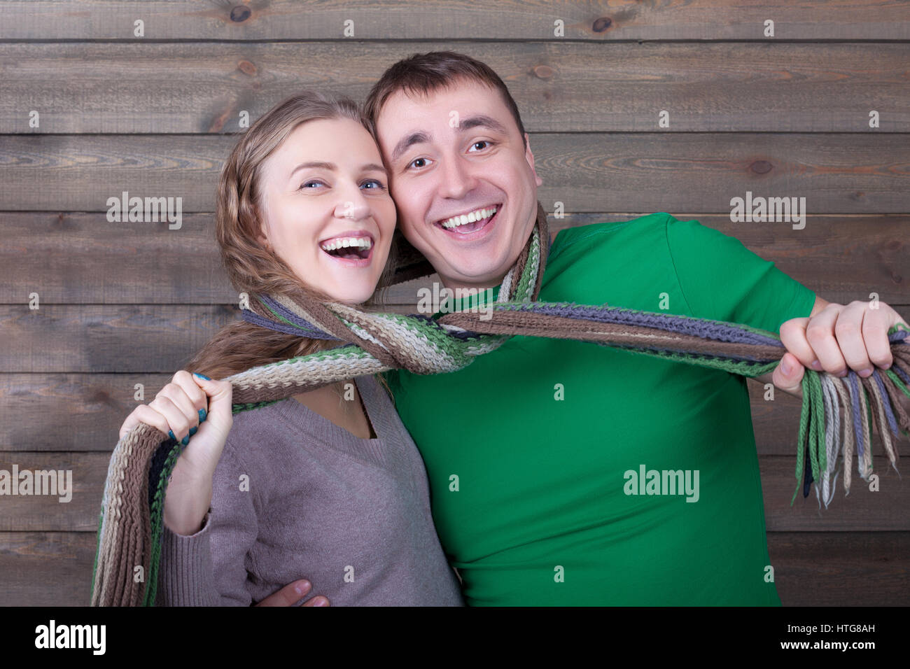 Smiling love couple wrapped in a scarf, wooden background. Funny photo ...