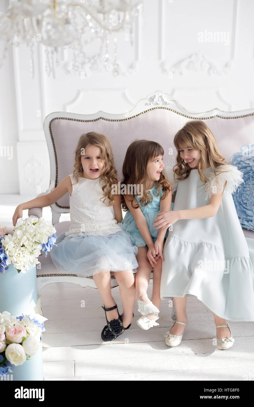 Portrait of three happy sisters sitting on sofa in photo studio. Luxury ...
