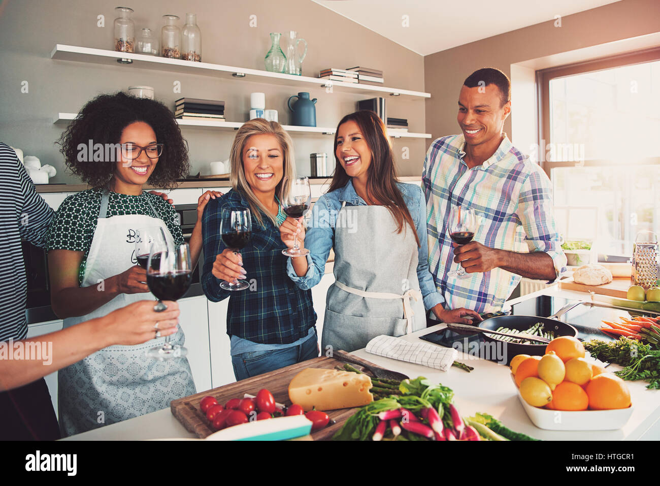 Group of young funny friends cheering with wine glasses while cooking ...