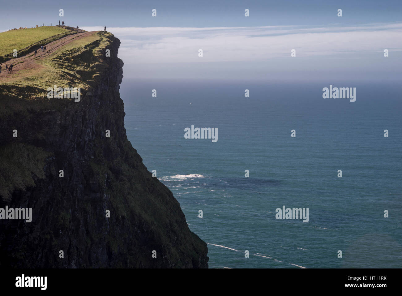 Tourists at the edge of vertical wall of Cliffs of Moher Stock Photo ...
