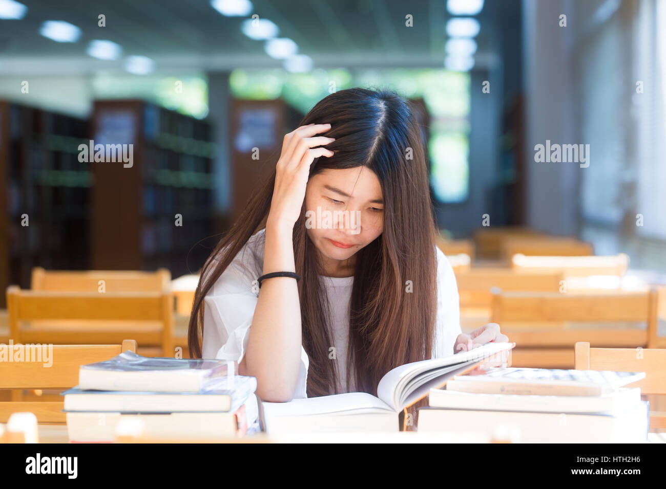 Portrait of a beautiful student reading book for exam in a library ...