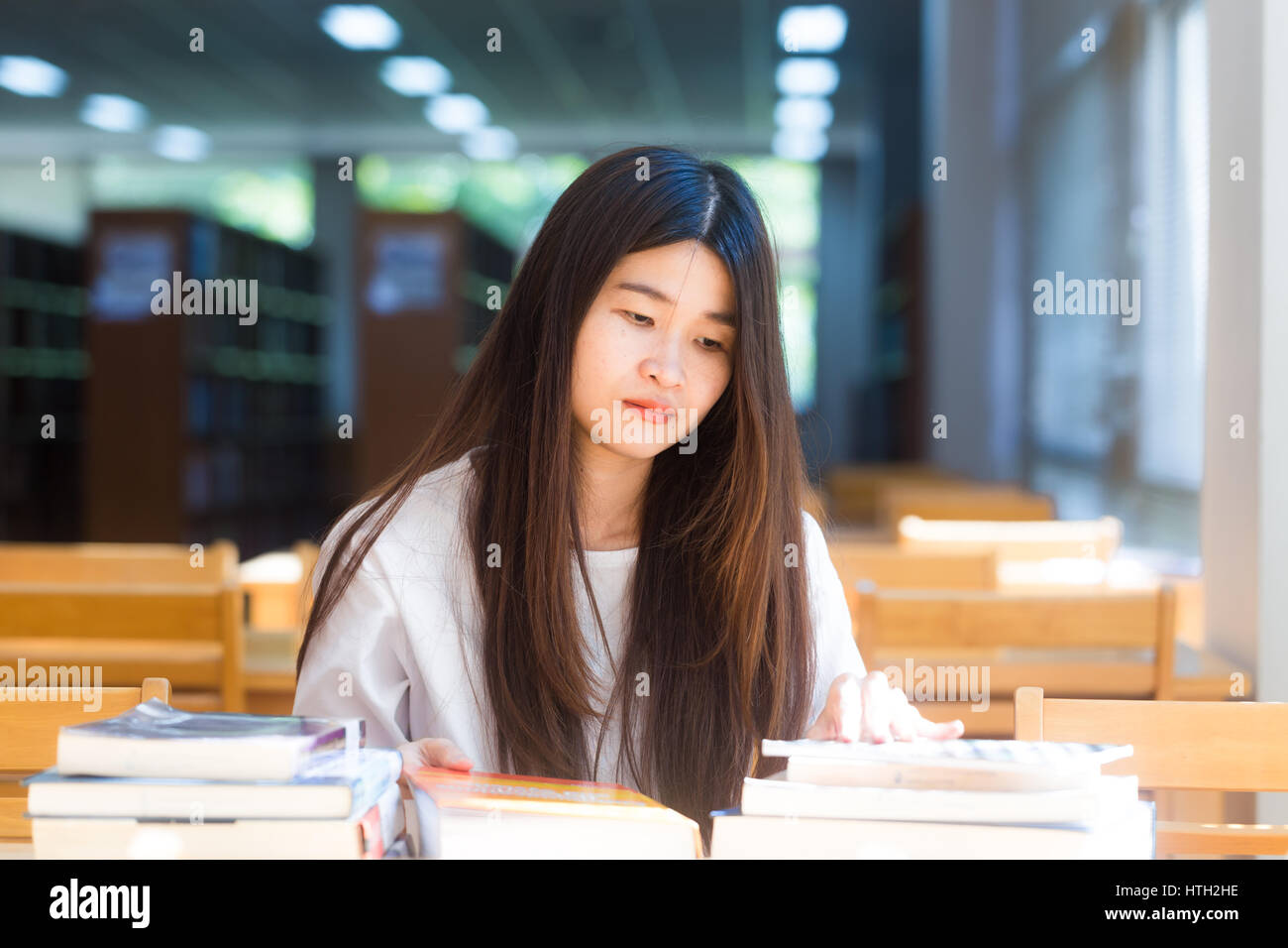 Portrait of a beautiful student reading book for exam in a library ...