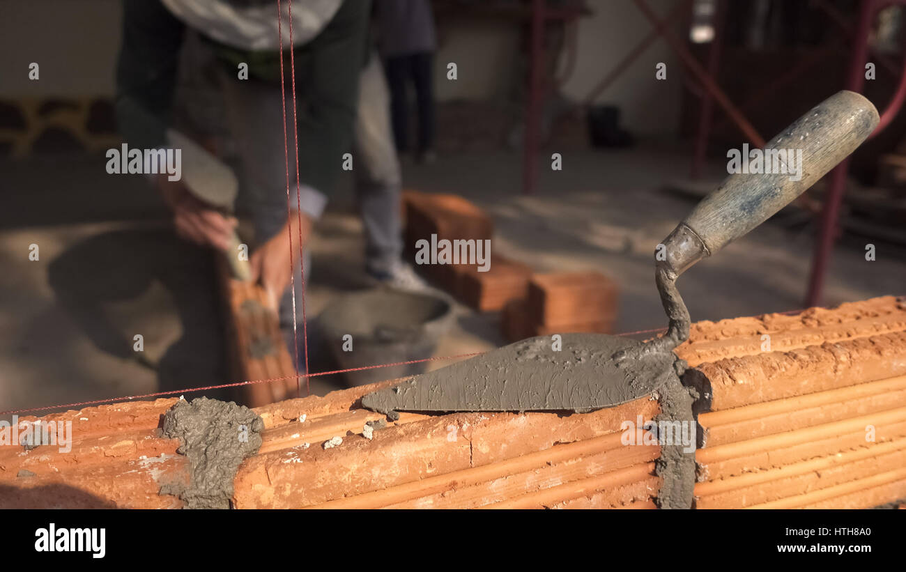 Bricklayer worker installing brick masonry on exterior wall with trowel ...