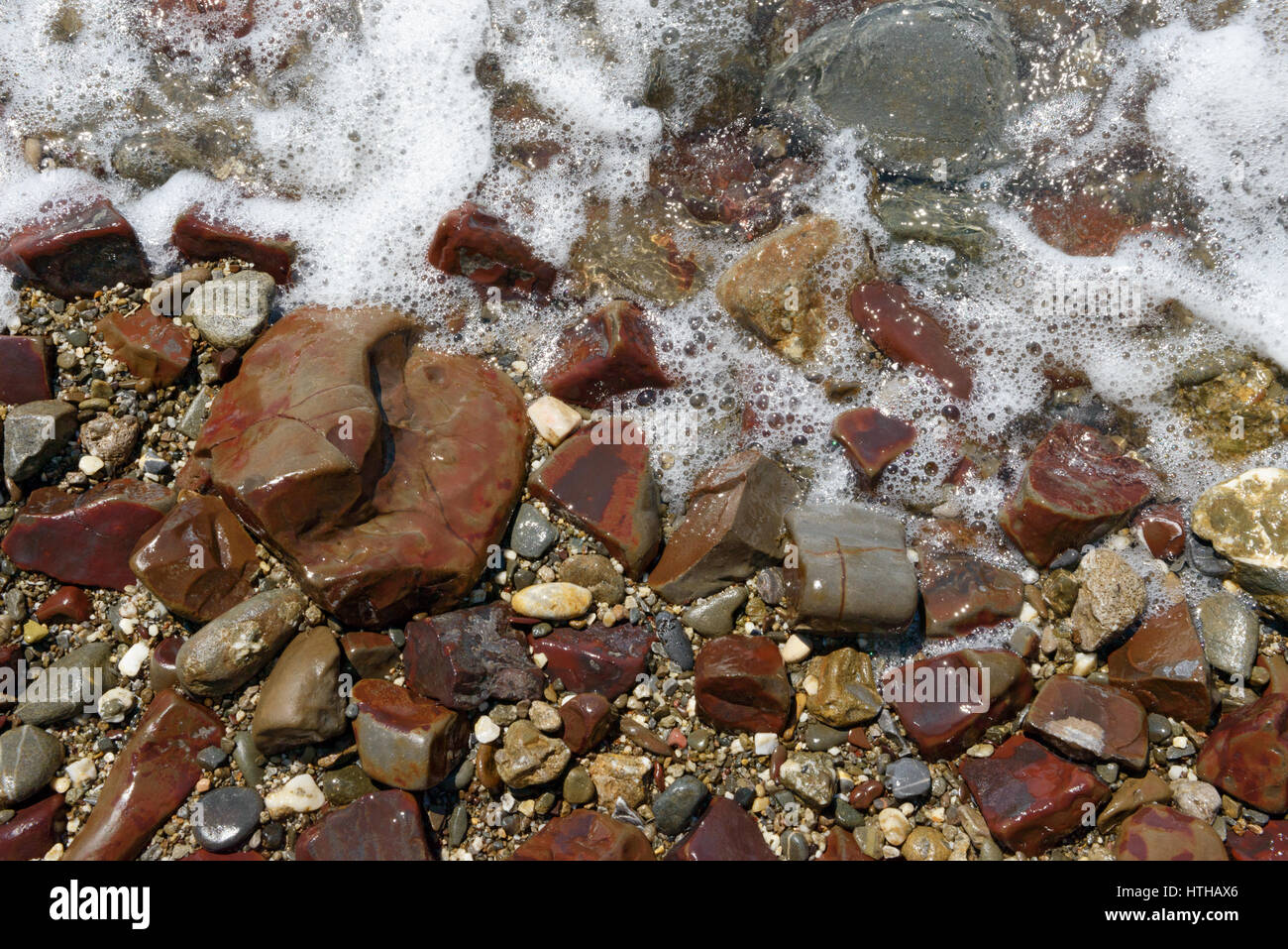 Close-up view of wet red stones and pebble of various colors under ...