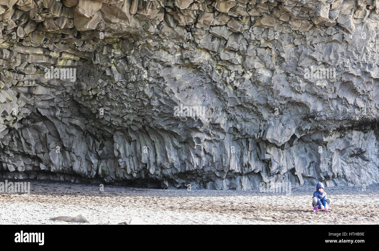 A small child looks small in comparison to high basalt cliff and large ...