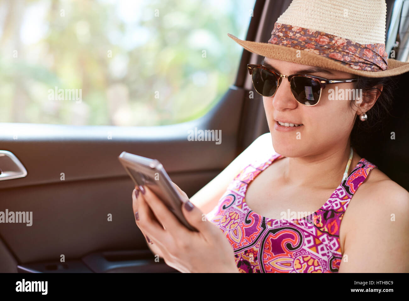 Woman in car sit with smartphone in hand. Girl using smartphone in back ...