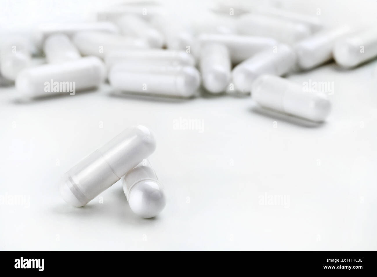 Two white capsules and heap of capsules on white background. High ...