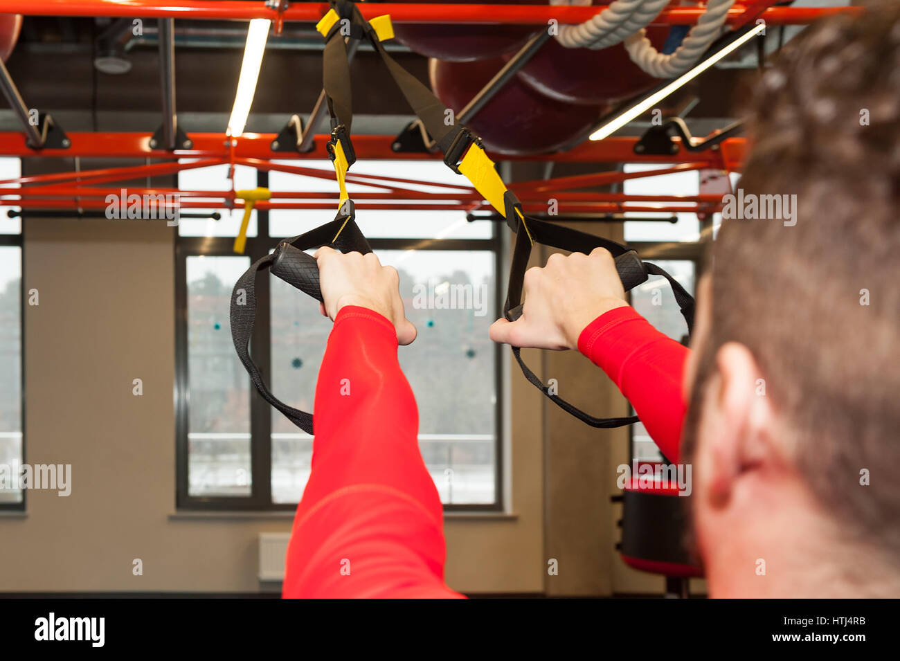 white curly bearded sporty man exercising with fitness straps in gym ...
