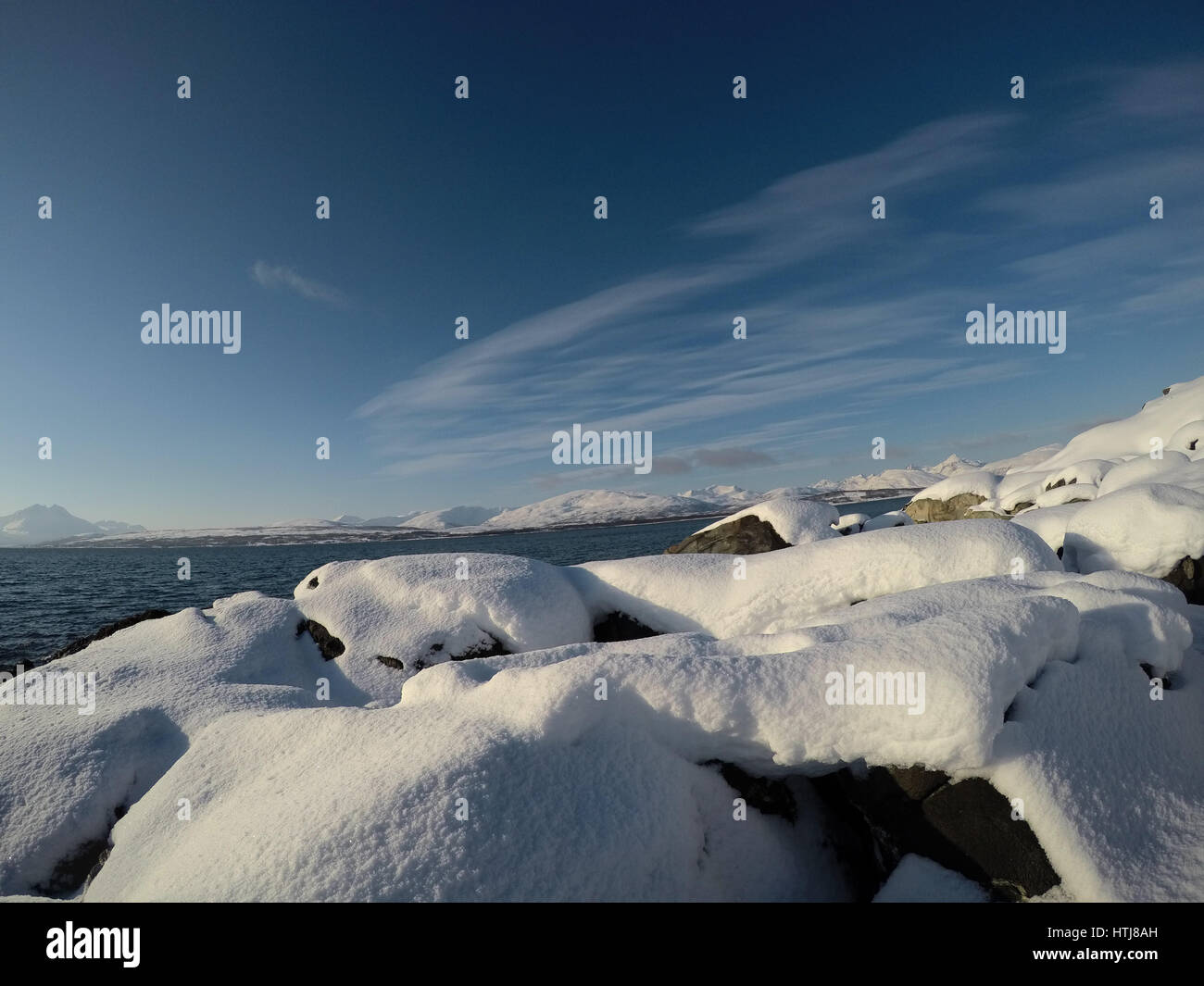deep snow on rocky sea shore with majestic blue sky, fjord and mountain ...