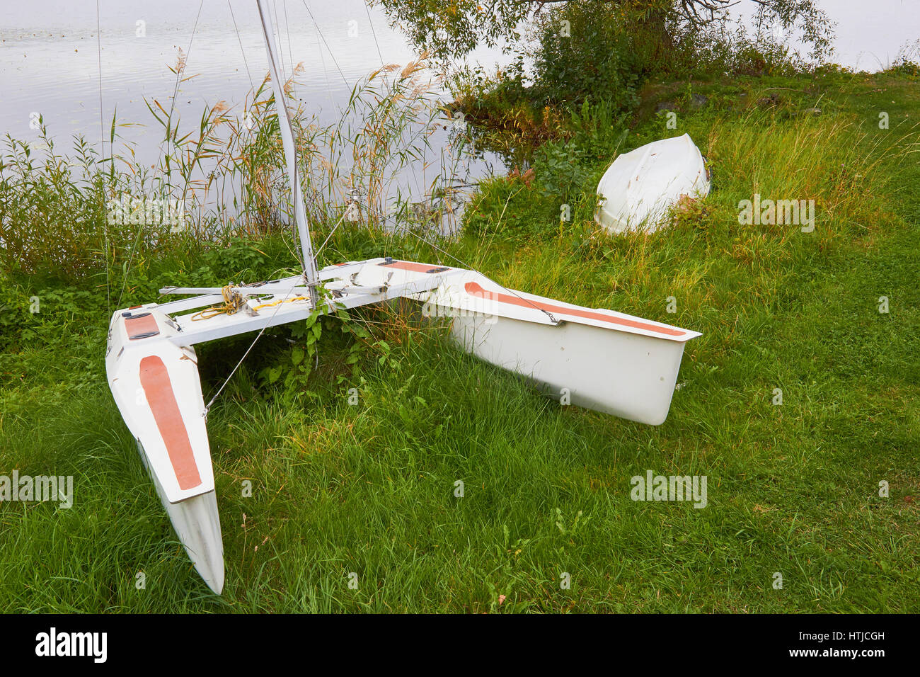 Catamaran and rowing boat in grass near waterfront, Sweden, Scandinavia ...