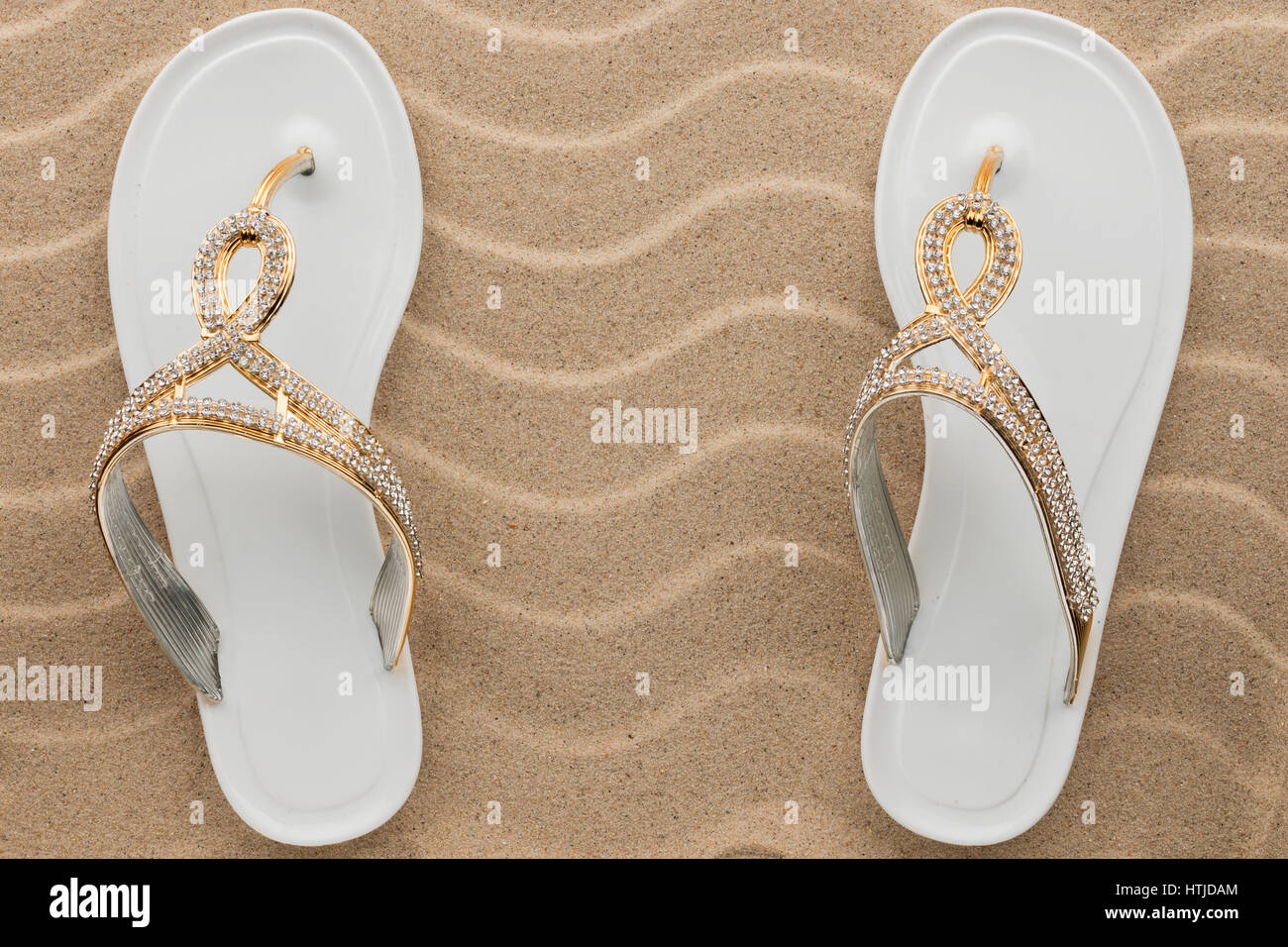 Pair of white beach sandals in rhinestones stand on the sand. View from ...