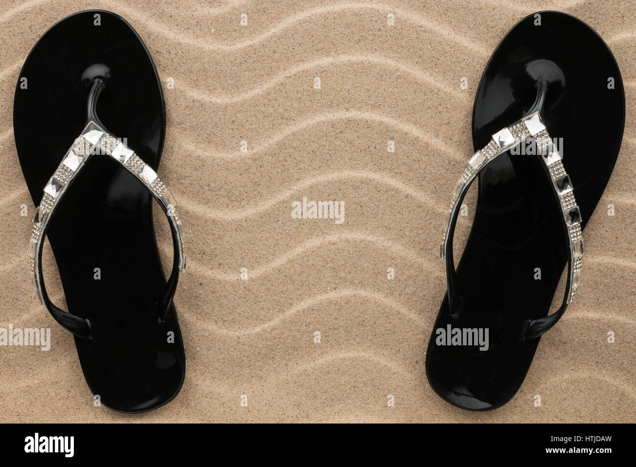Pair of black beach sandals in rhinestones stand on the sand. View from ...