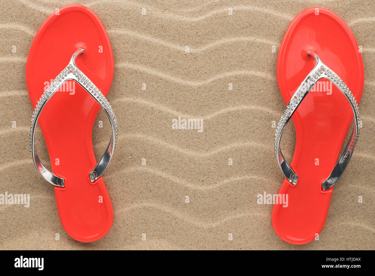 Pair of red beach sandals in rhinestones stand on the sand. View from ...
