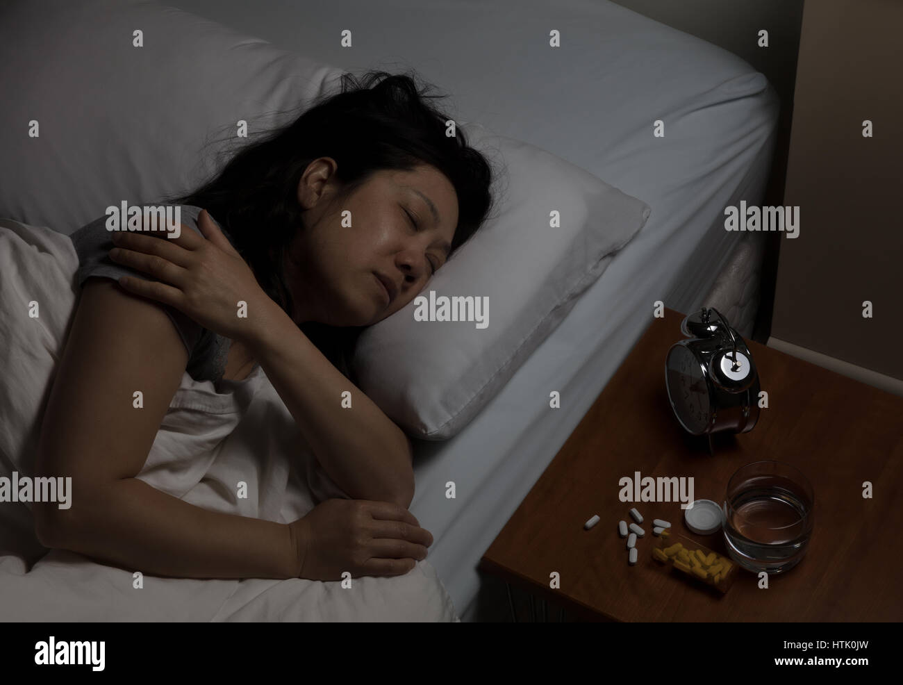 Mature woman holding shoulder while in pain with pills spilled on night ...