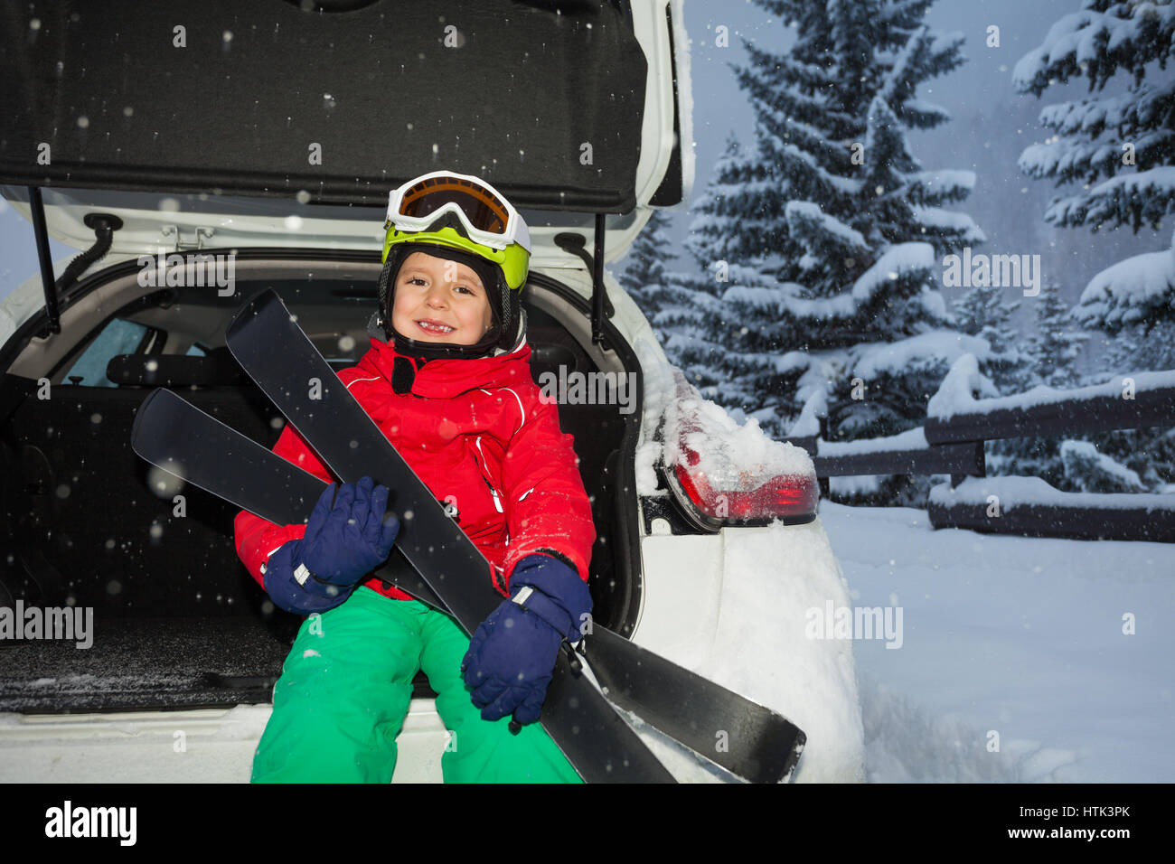 Happy boy in safety helmet and mask sitting in car trunk after ski trip ...