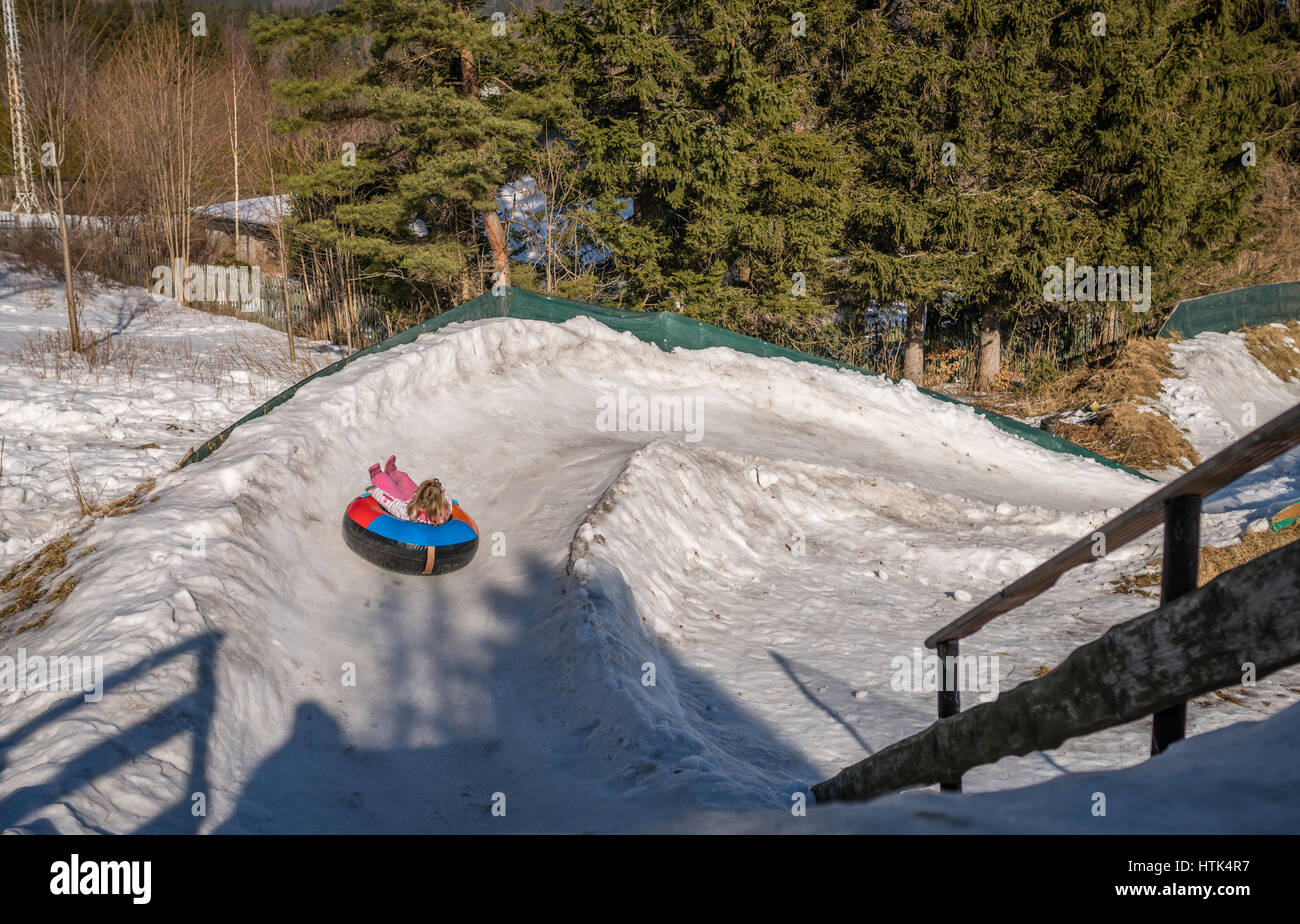 Little girl sledding downhill a snowy and icy hill track on a colorful ...