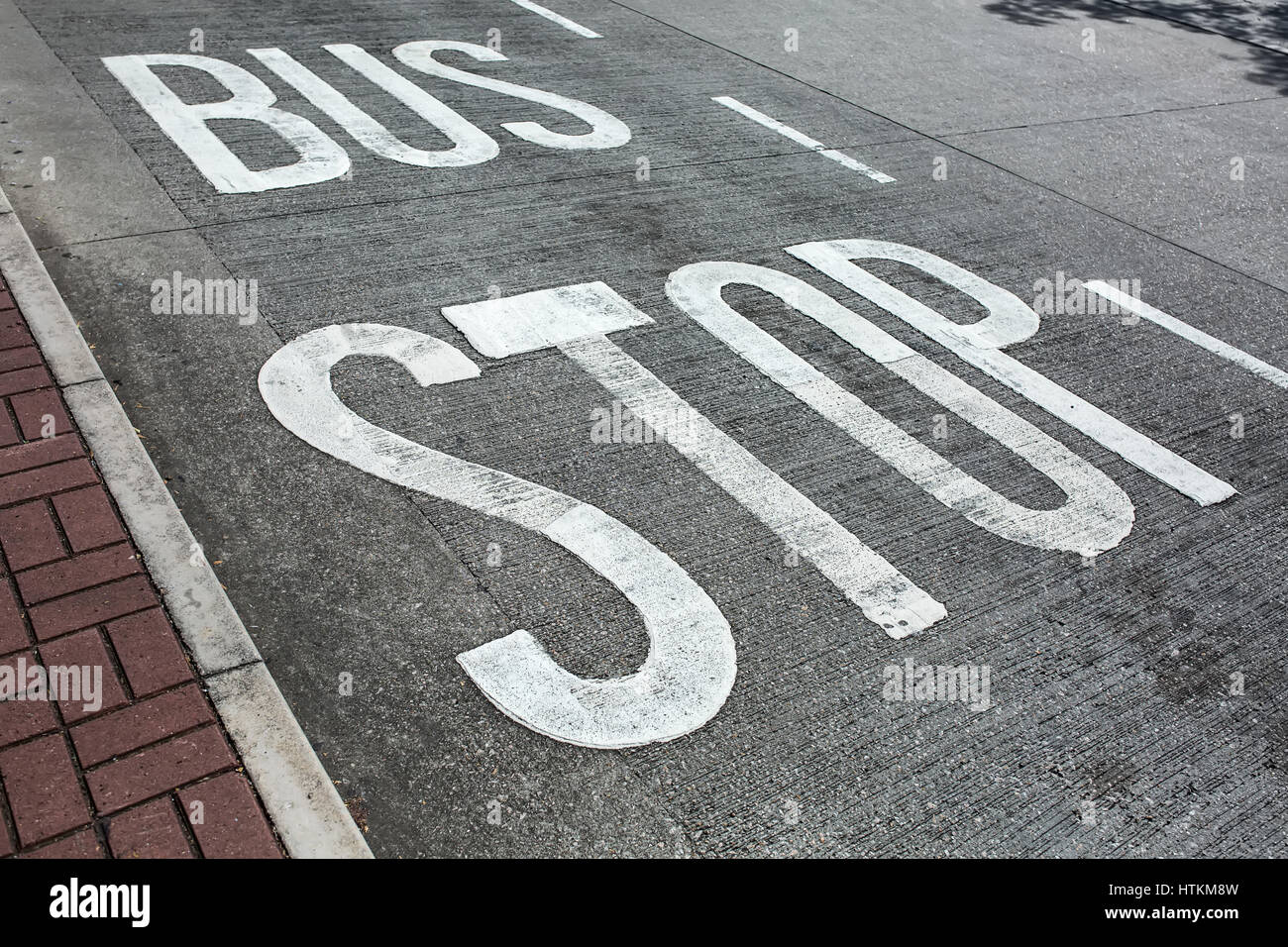 Part of the roadway and sidewalk. There is a Bus Stop white inscription ...