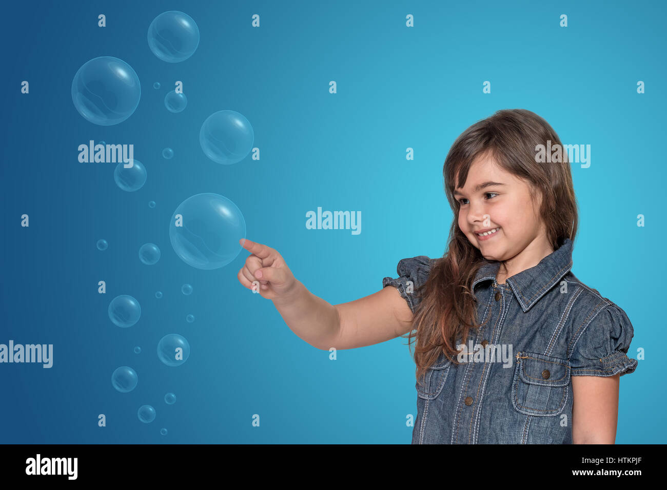 Smiling little girl is touching the transparent bubbles. All is on on ...
