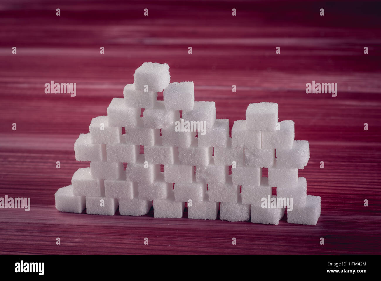 The wall built of sugar cubes on the red wooden table Stock Photo - Alamy