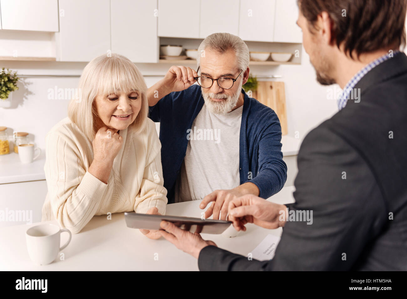 Cheerful retired couple using gadget with real estate agent Stock Photo ...