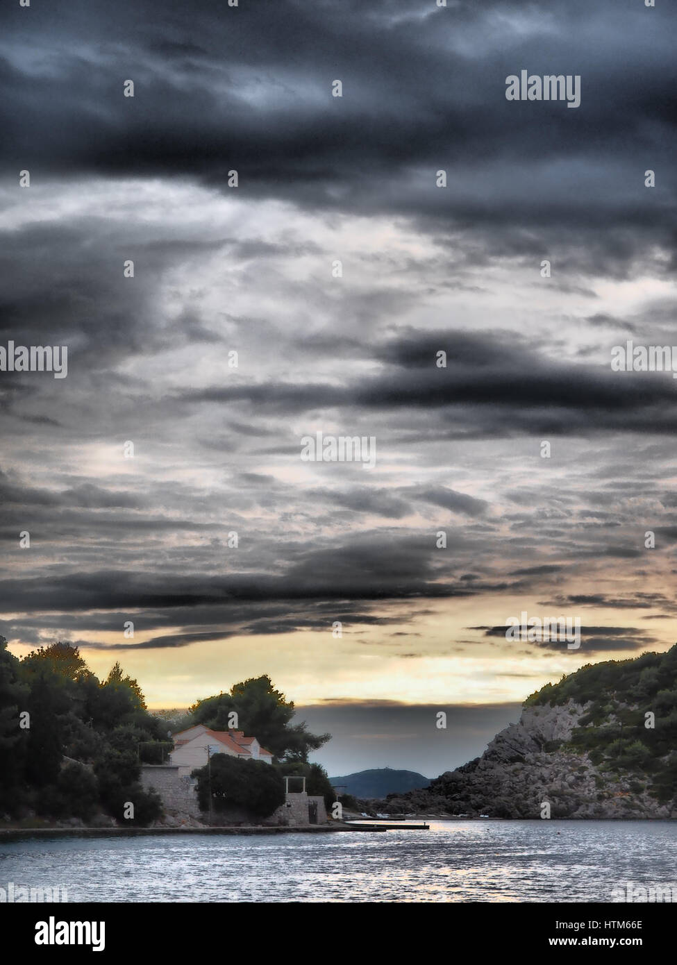 An angry stormy storm dark sky with clouds above a rocky island outcrop ...