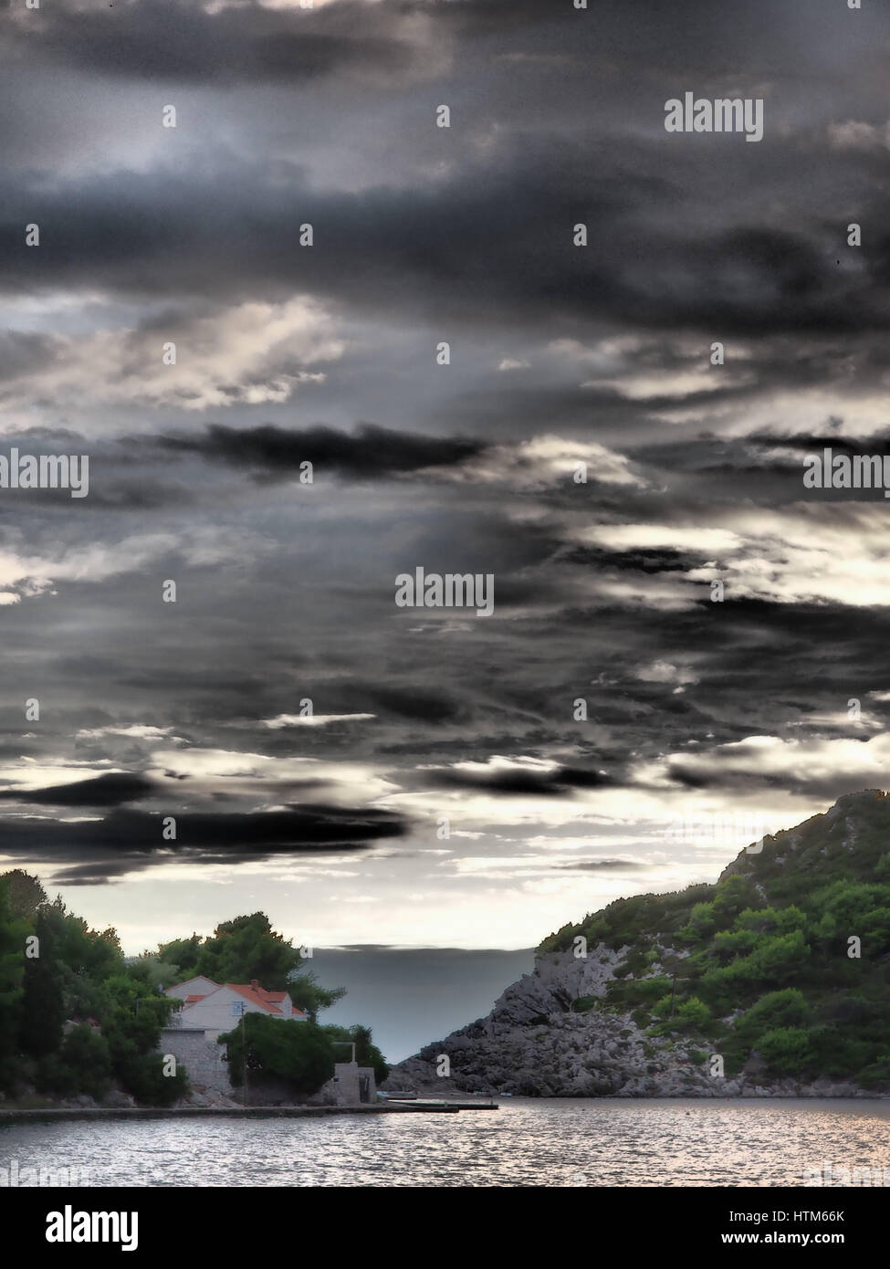 An angry stormy storm dark sky with clouds above a rocky island outcrop ...