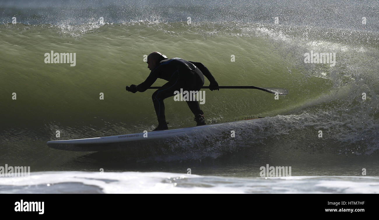 A paddle border surfs a wave on Boscombe beach in Bournemouth, Dorset ...