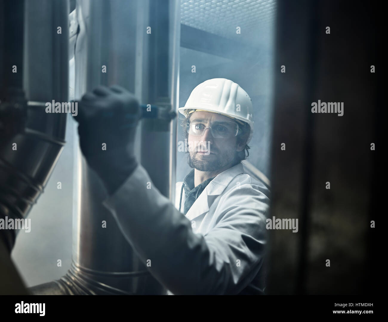 Mechanic with white helmet and lab coat moving a lever of a refrigerant ...