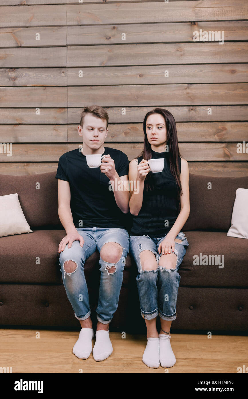 sad couple sitting on a brown sofa, look askance at each other and ...