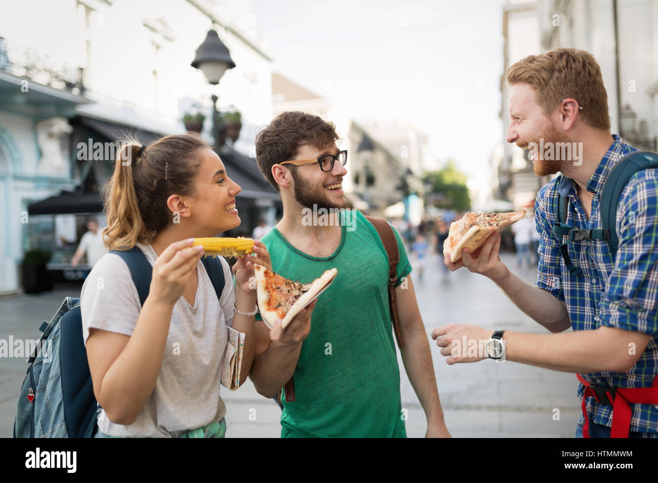 Happy people eating fast food in city while travelling with backpacks ...